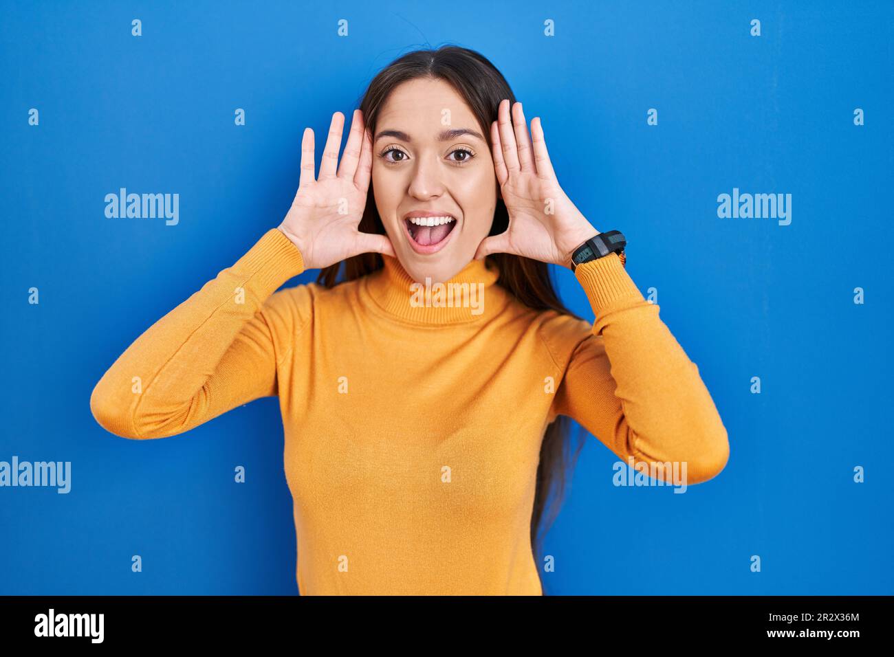 Young brunette woman standing over blue background smiling cheerful ...