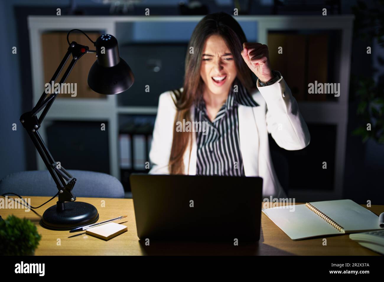 Young brunette woman working at the office at night with laptop angry ...