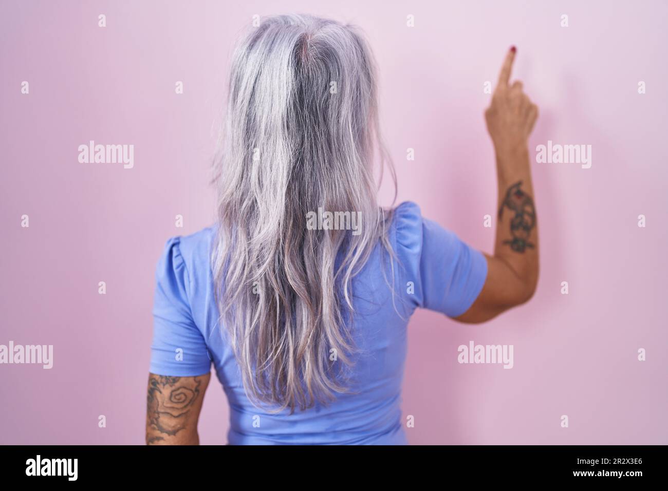 Middle age woman with tattoos standing over pink background posing ...