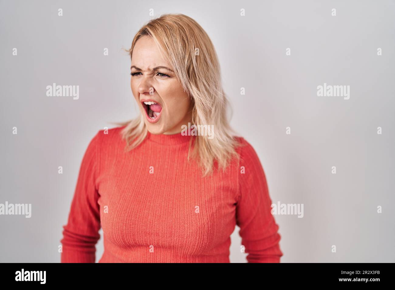 Blonde woman standing over isolated background angry and mad screaming ...