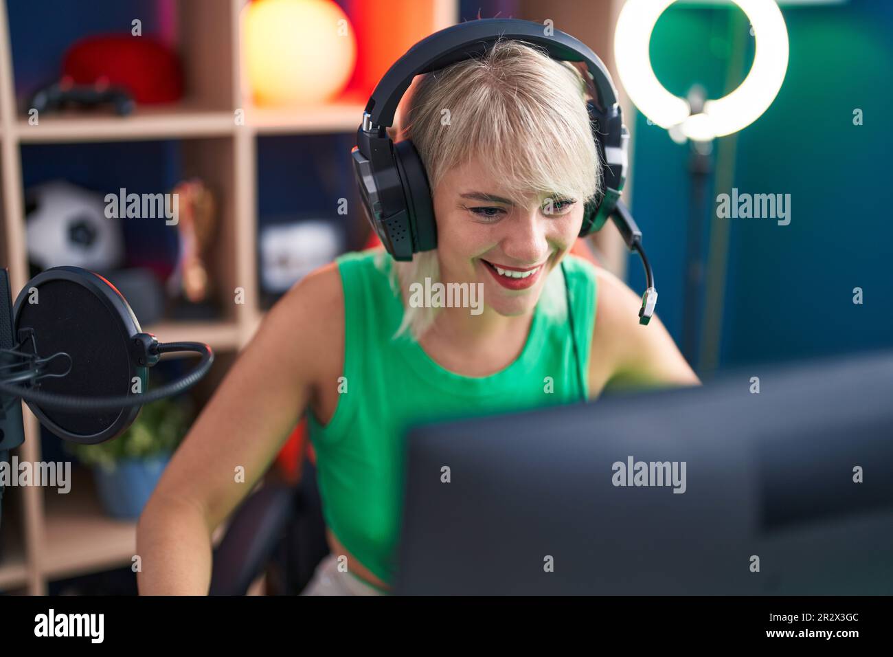 Young blonde woman streamer playing video game using computer at gaming ...