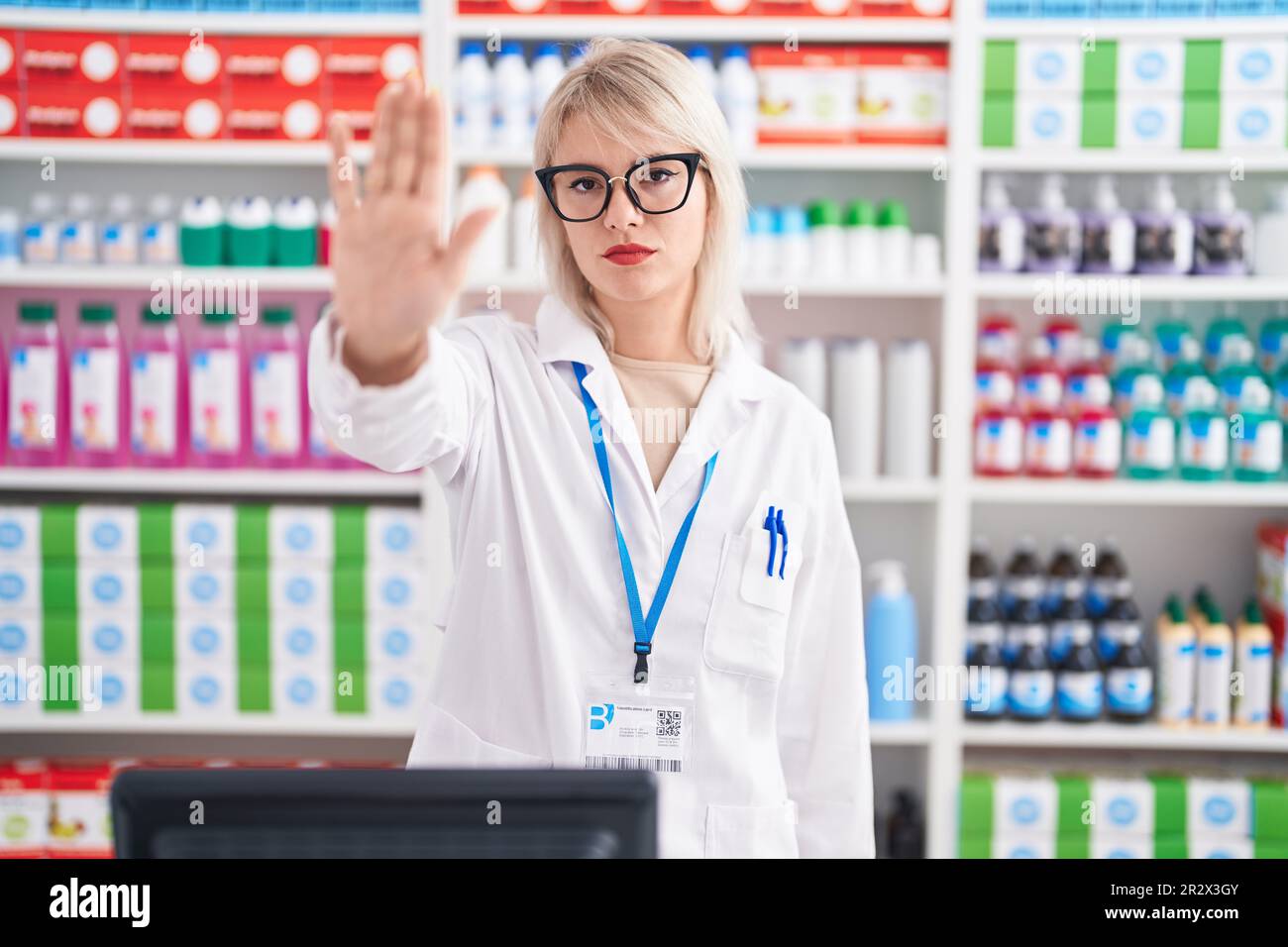Young caucasian woman working at pharmacy drugstore doing stop sing ...