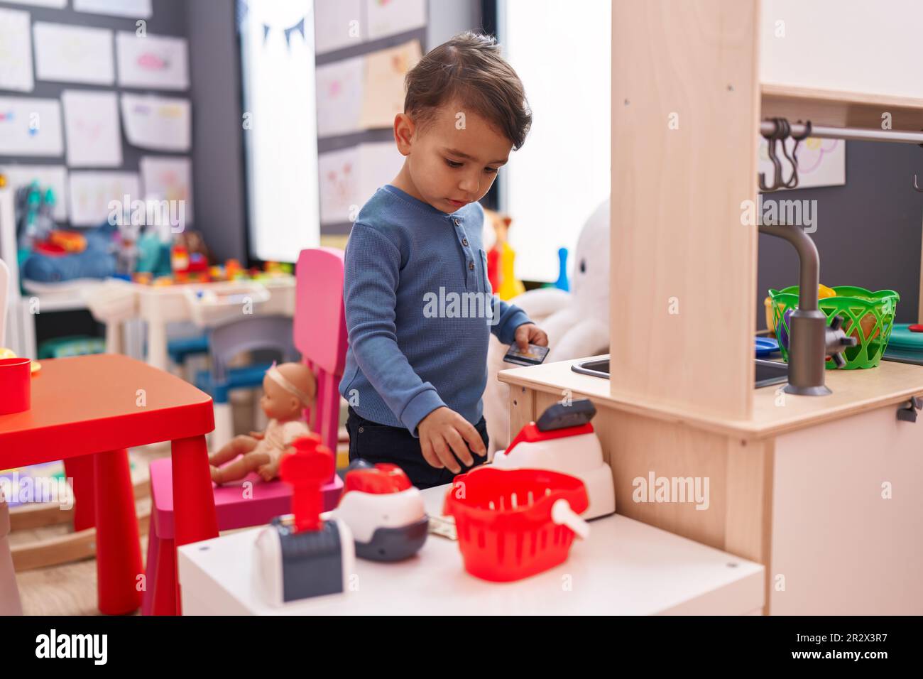 Adorable hispanic boy playing supermarket game standing at kindergarten ...