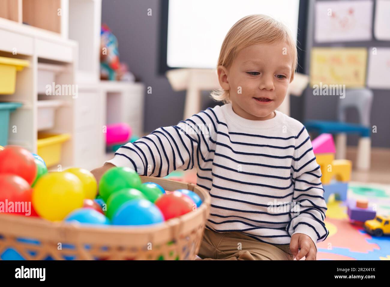 Adorable caucasian boy playing with balls sitting on floor at ...