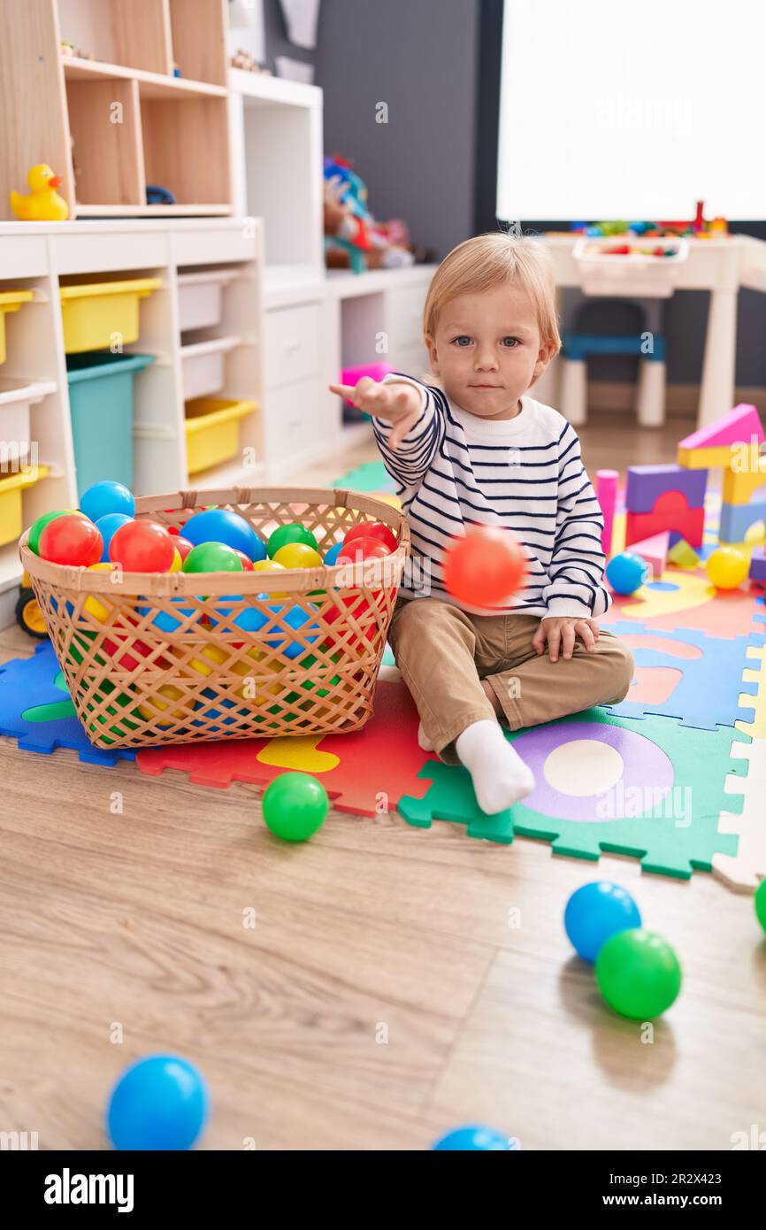 Adorable caucasian boy playing with balls sitting on floor at ...