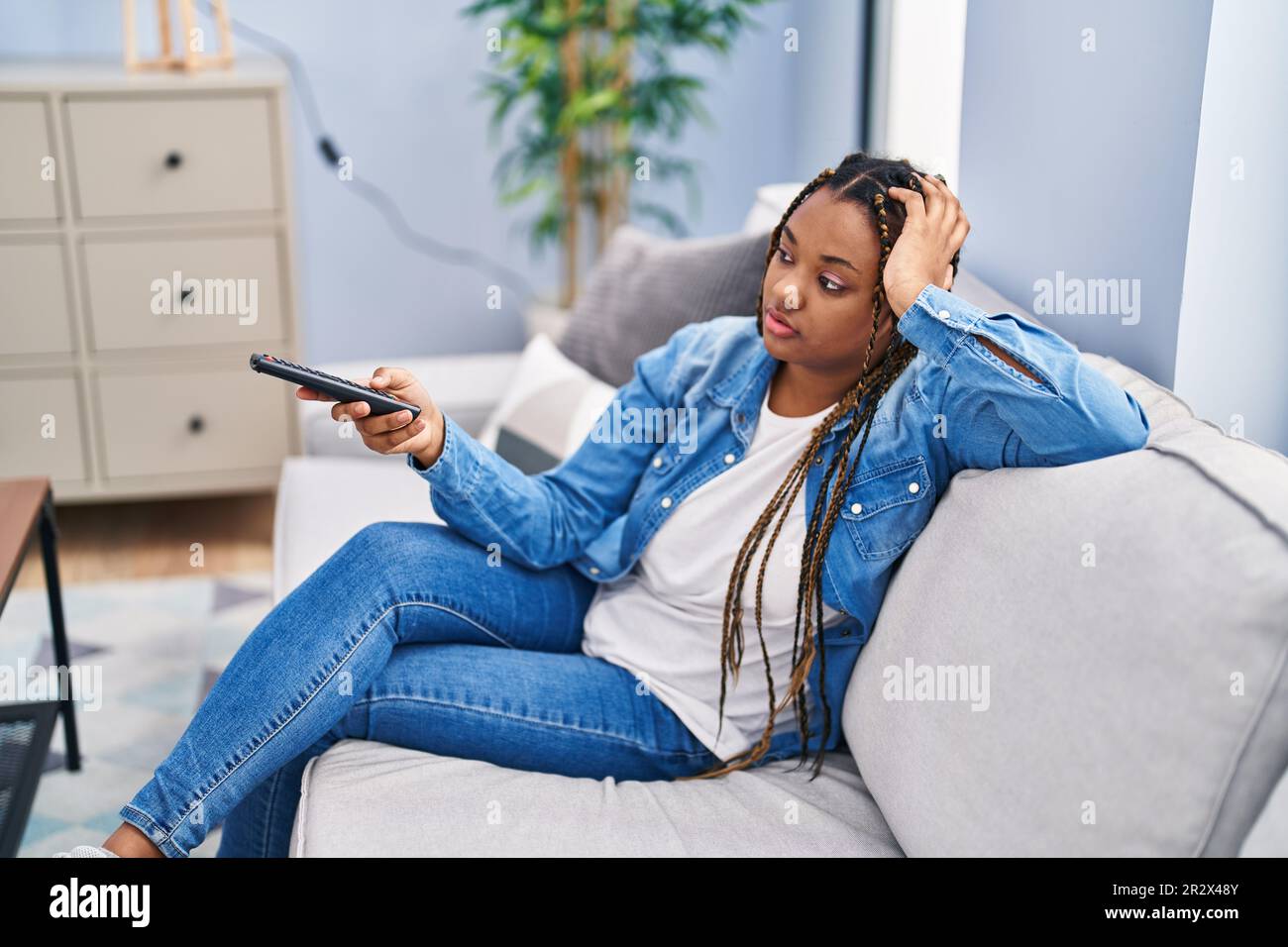 African american woman watching tv sitting on sofa with boring ...