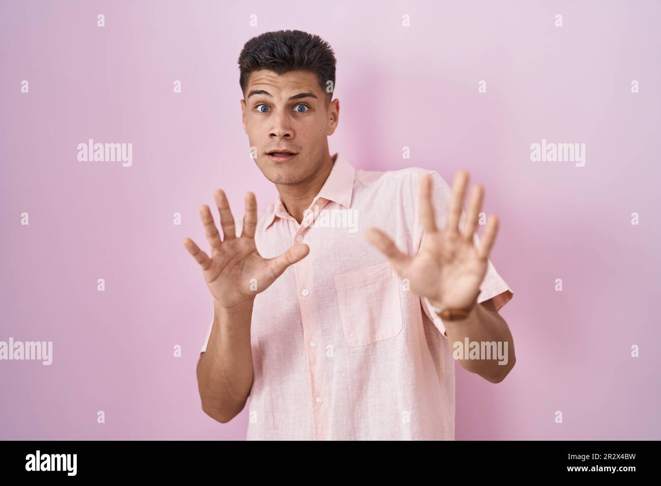 Young hispanic man standing over pink background afraid and terrified ...