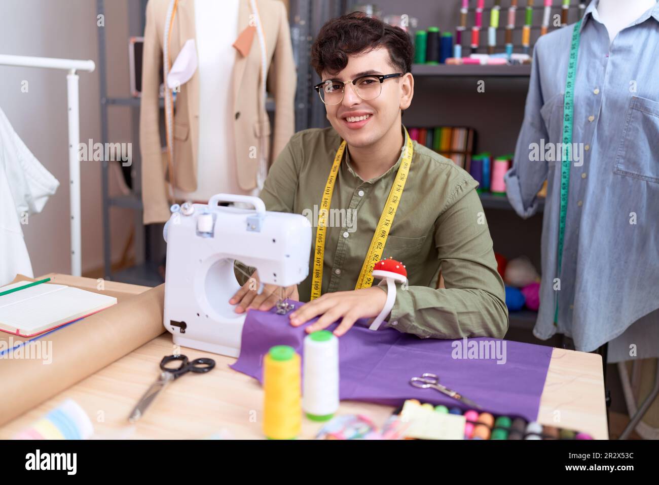 Non binary man tailor smiling confident using sewing machine at atelier ...