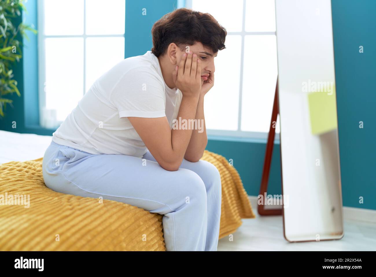 Non binary man stressed sitting on bed at bedroom Stock Photo - Alamy