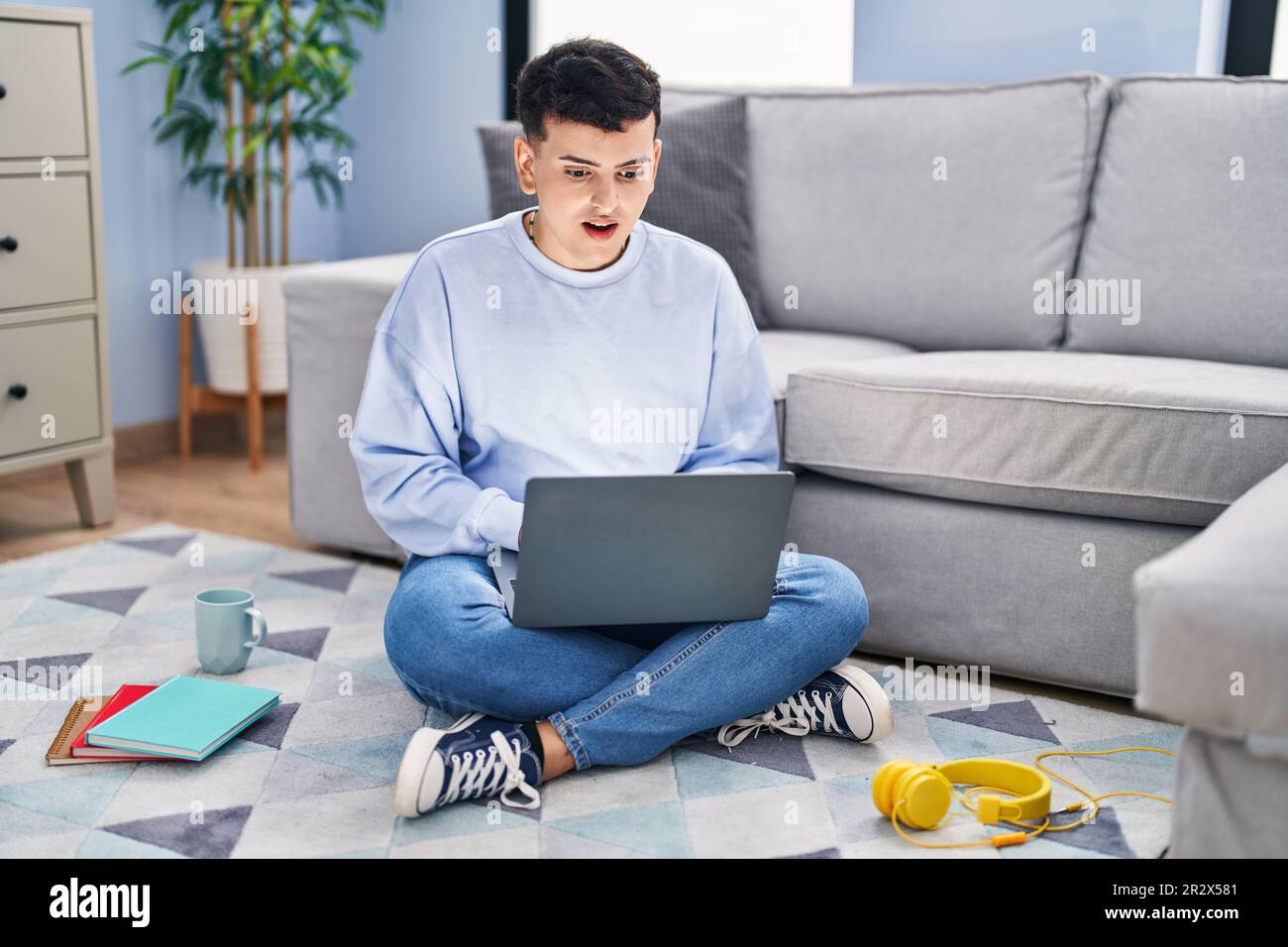 Non binary person studying using computer laptop sitting on the floor ...