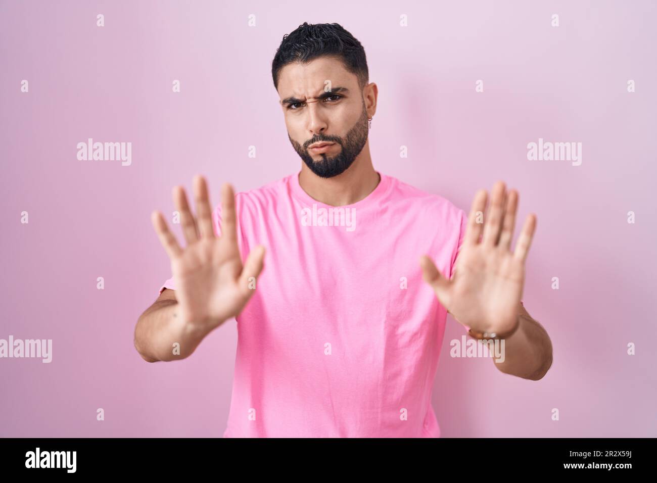 Hispanic young man standing over pink background moving away hands ...