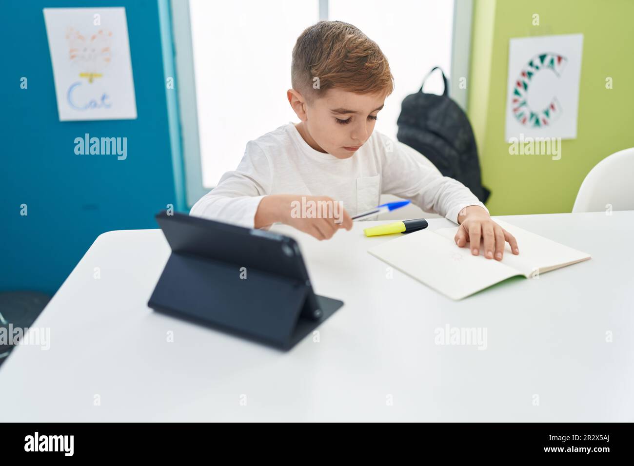 Adorable hispanic boy student using touchpad writing notes at classroom ...