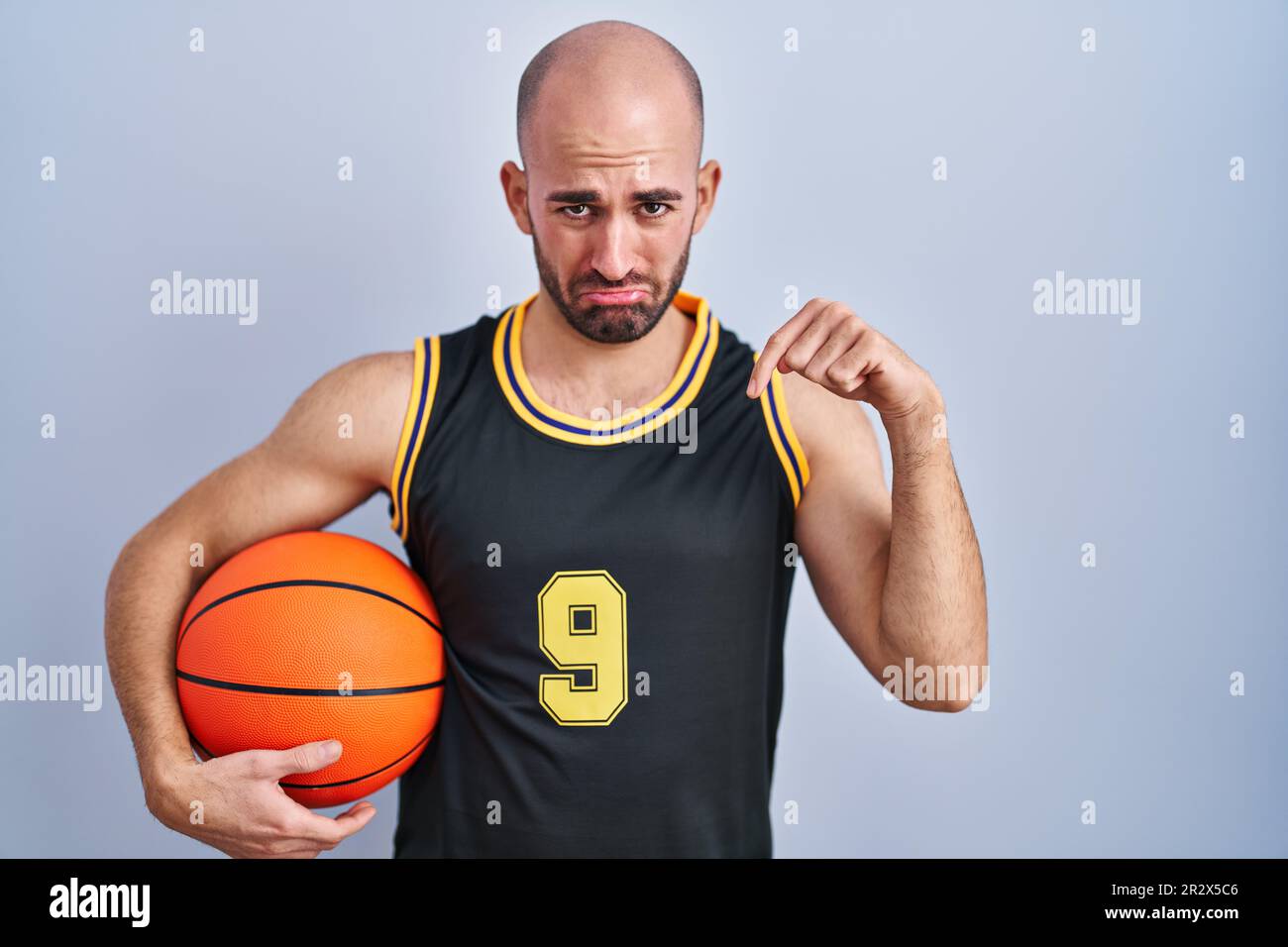 Young bald man with beard wearing basketball uniform holding ball ...