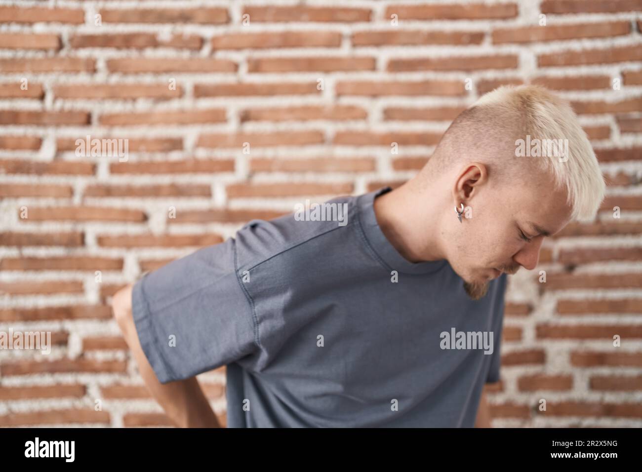 Young caucasian man standing over bricks wall suffering of backache ...