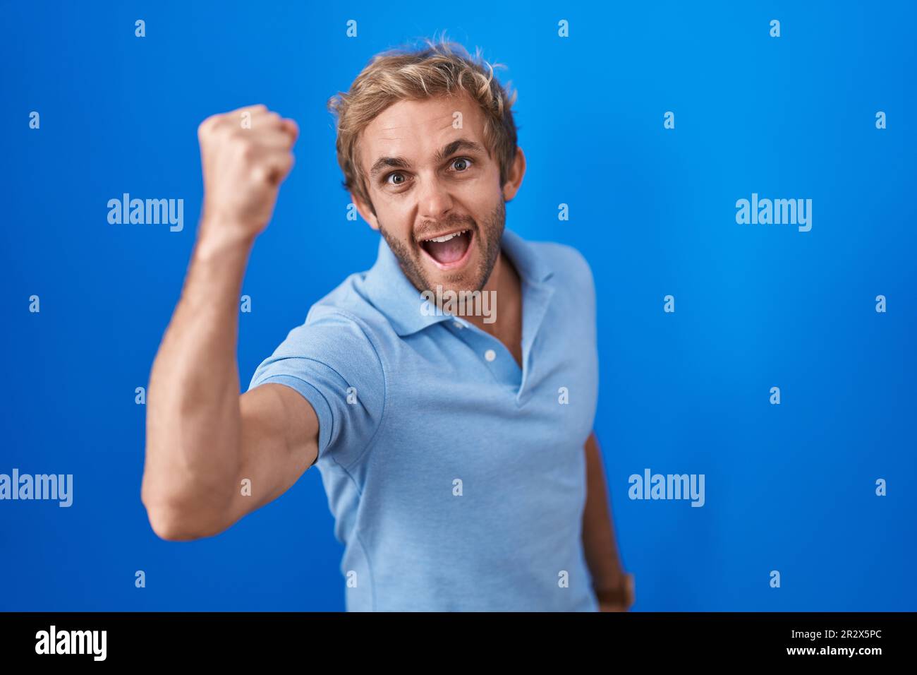 Caucasian man standing over blue background angry and mad raising fist ...