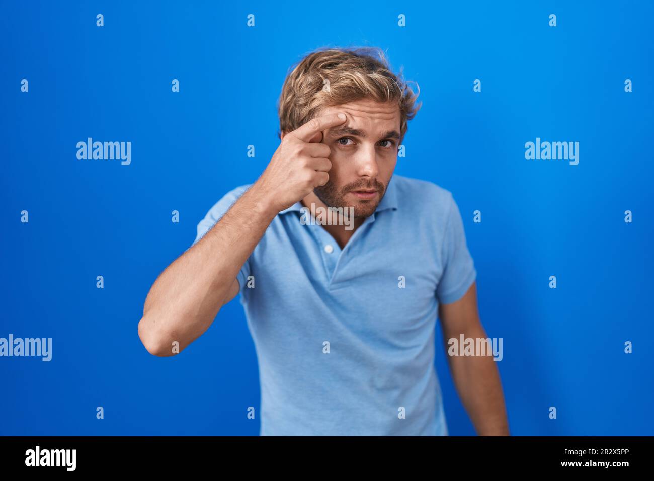 Caucasian man standing over blue background pointing unhappy to pimple ...