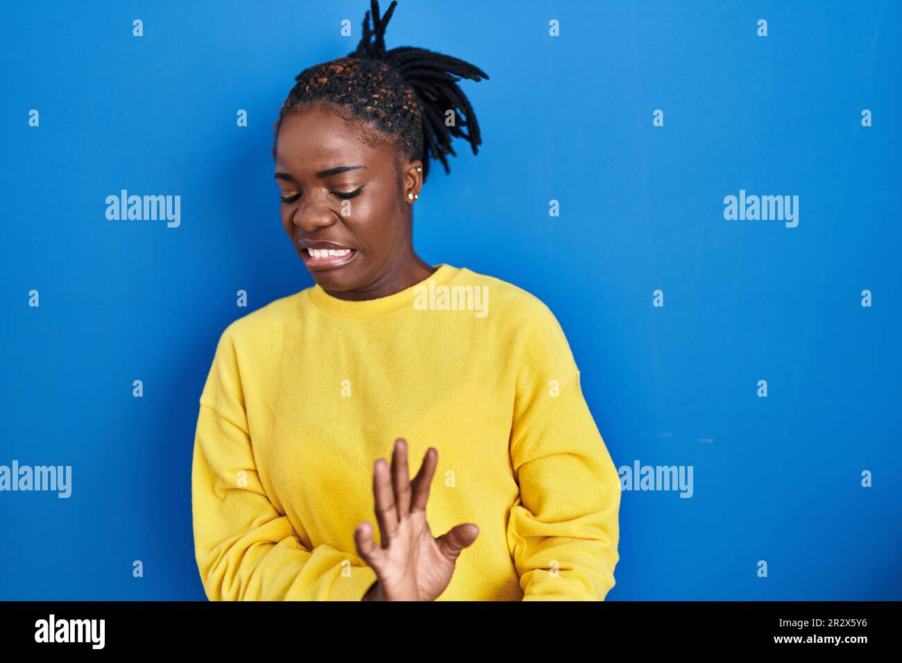 Beautiful black woman standing over blue background disgusted ...