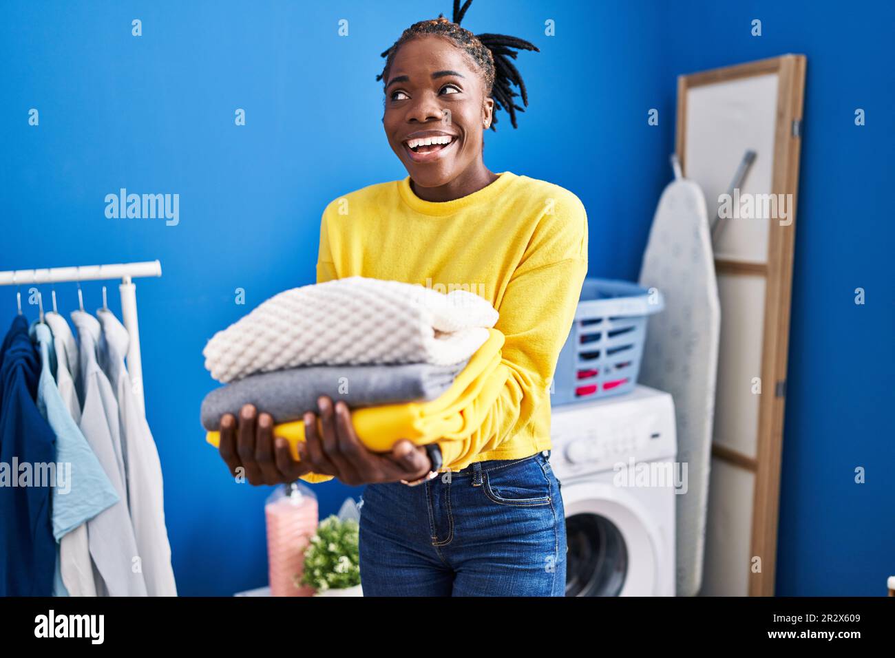Beautiful black woman holding clean laundry celebrating crazy and amazed for success with open ...
