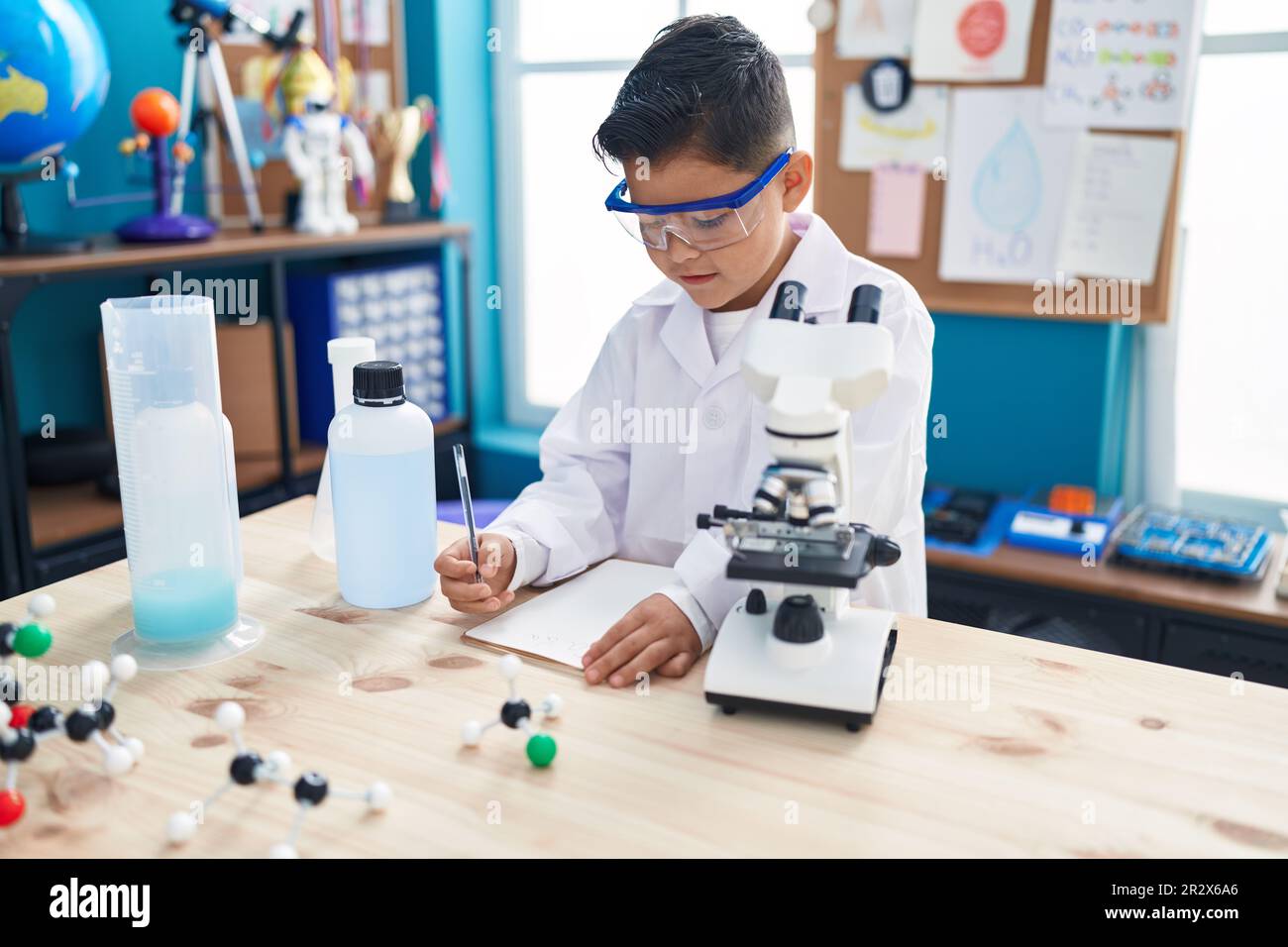 Adorable hispanic boy student using microscope writing notes at ...