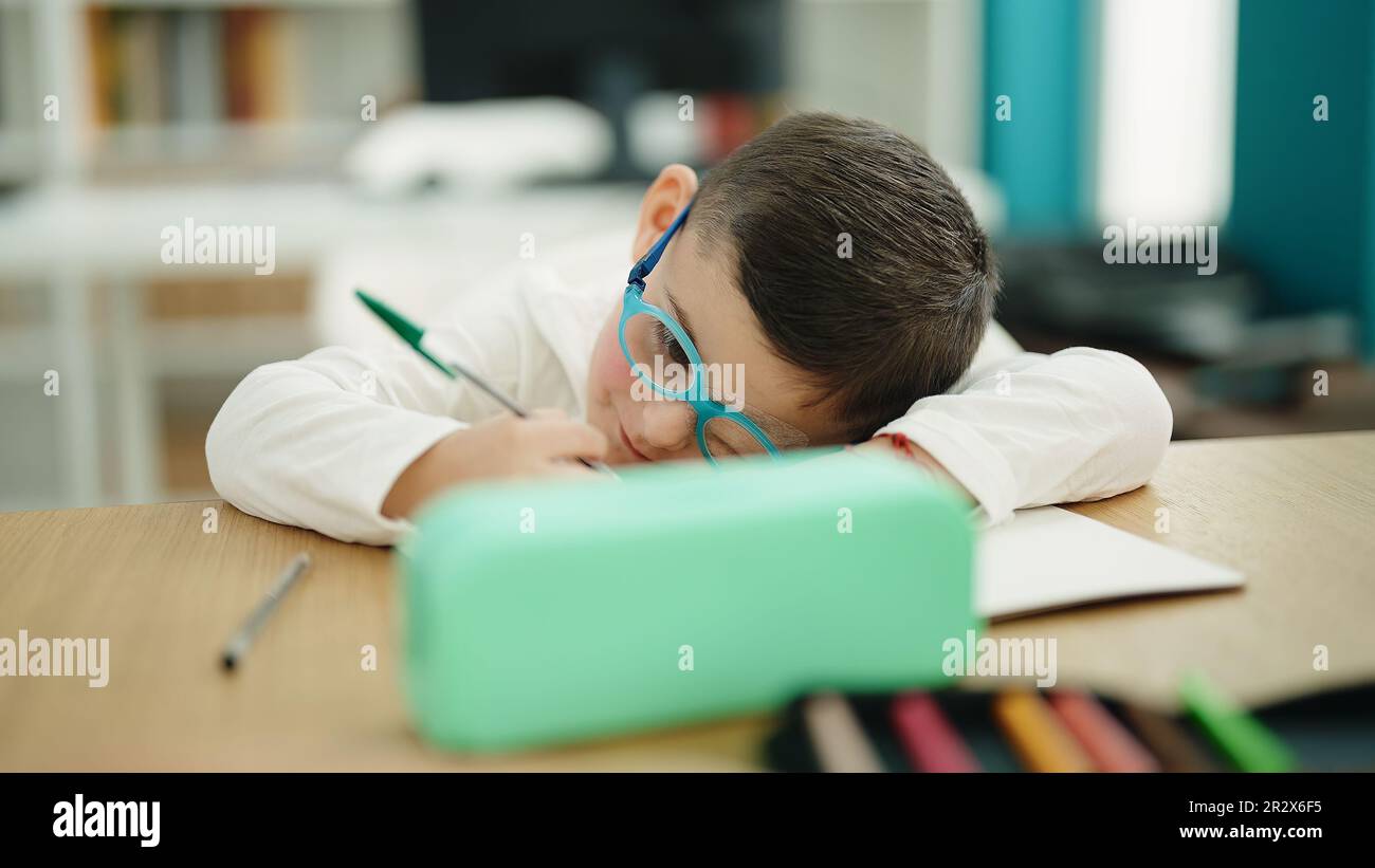 Adorable hispanic boy student writing notes tired at classroom Stock ...