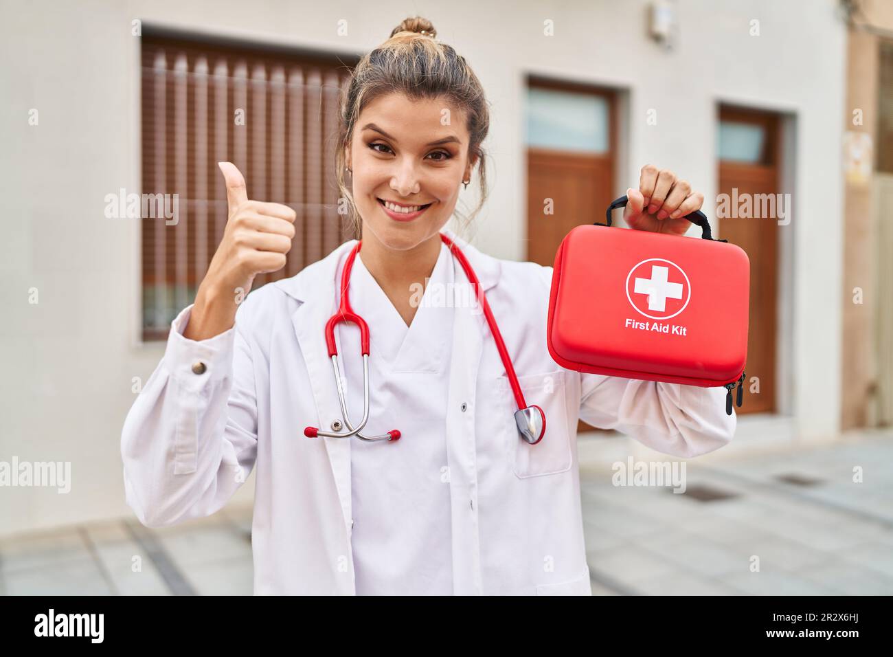 Young doctor woman holding first aid kit smiling happy and positive ...