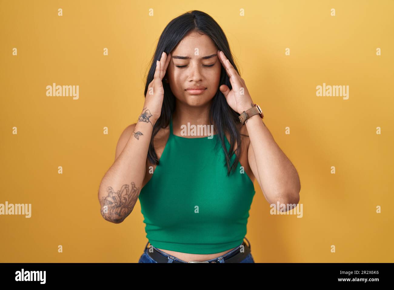 Brunette woman standing over yellow background with hand on head ...