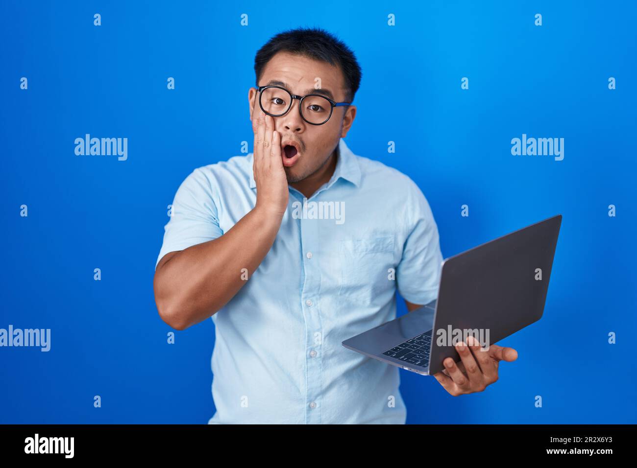 Chinese young man using computer laptop afraid and shocked, surprise ...