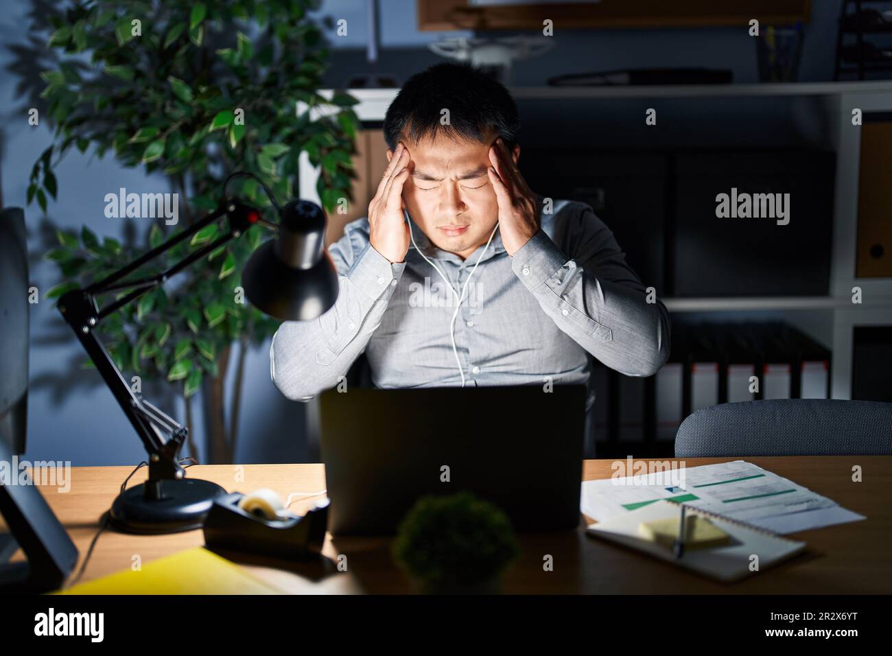 Young chinese man working using computer laptop at night with hand on ...