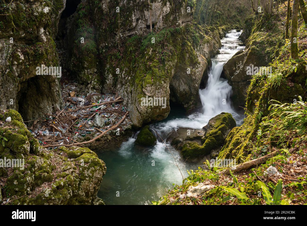Waterfall with mossy rocks in mountain canyon and plastic waste problem ...