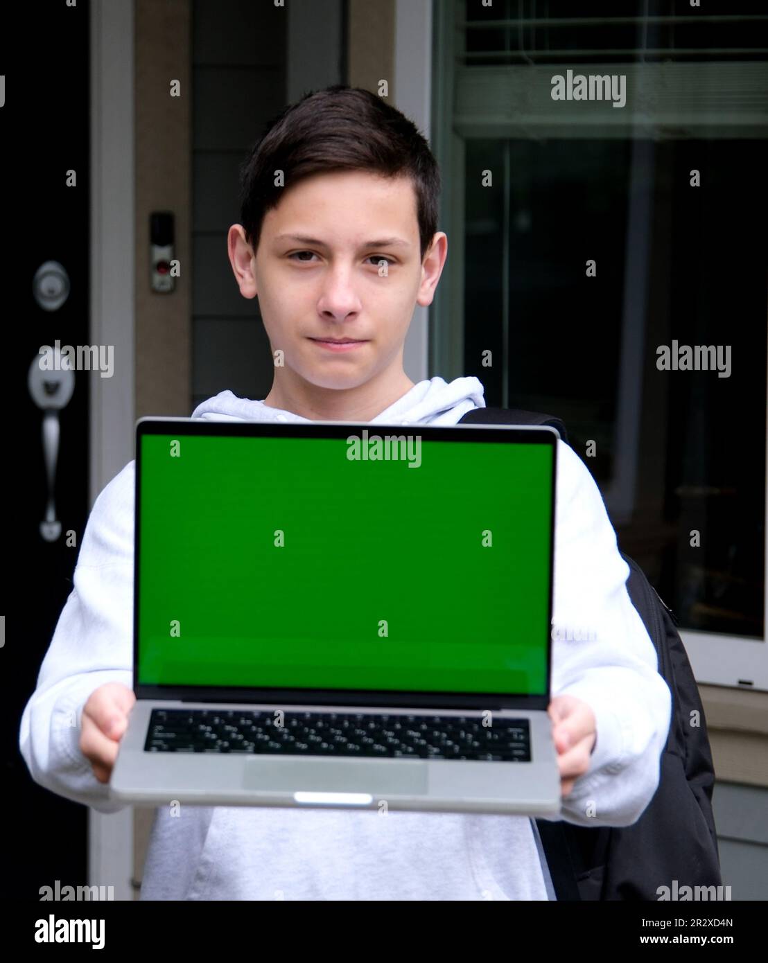teenage boy in gray hoodie holding laptop with green screen product ...