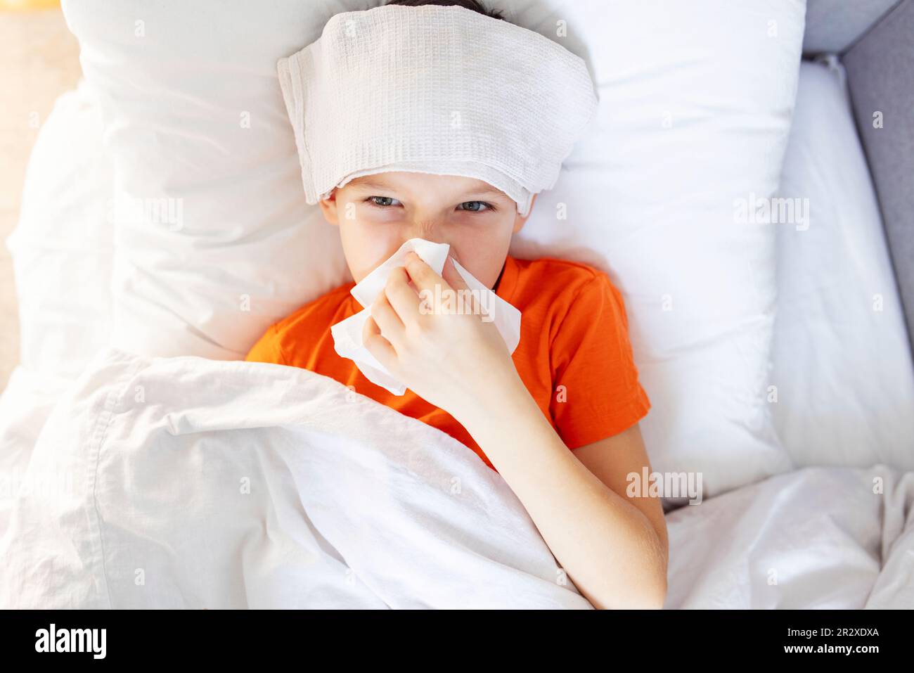 Sick child boy is lying in bed with high fever and blowing his nose ...