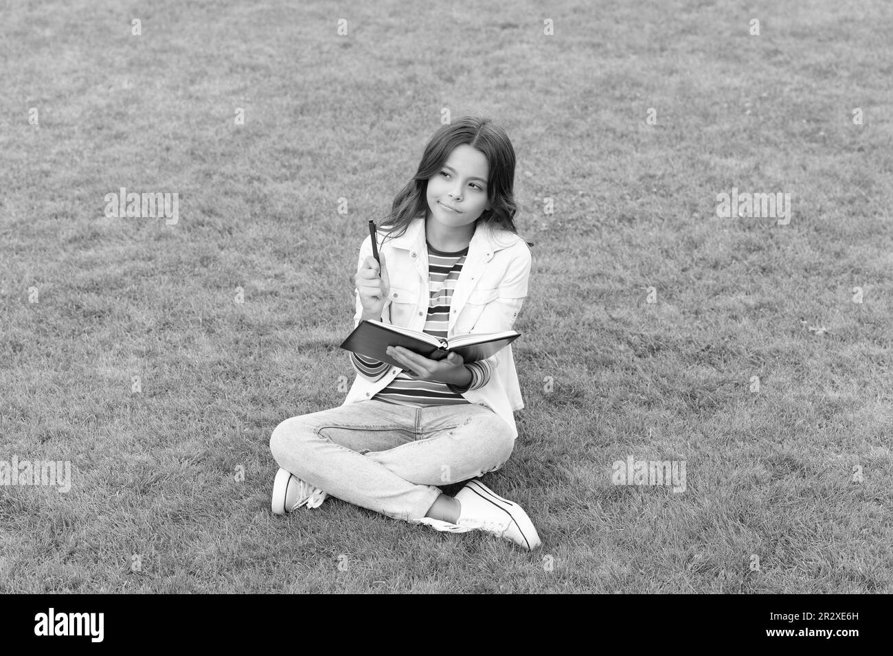 thoughtful teen child making notes in notebook sitting on grass. taking ...