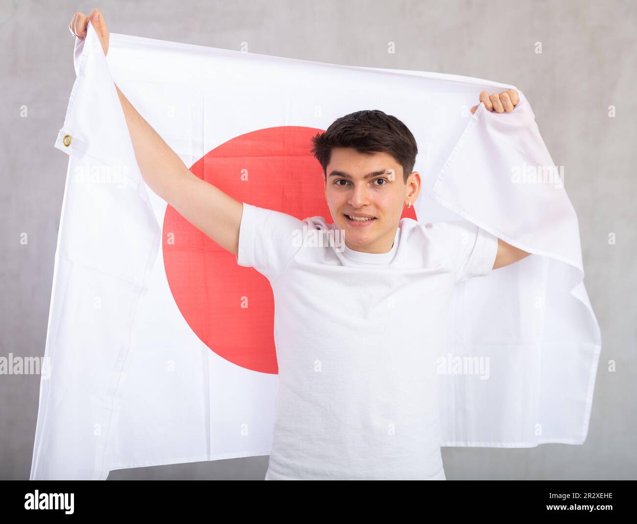 Happy young man holding flag of Japan against unicoloured background ...