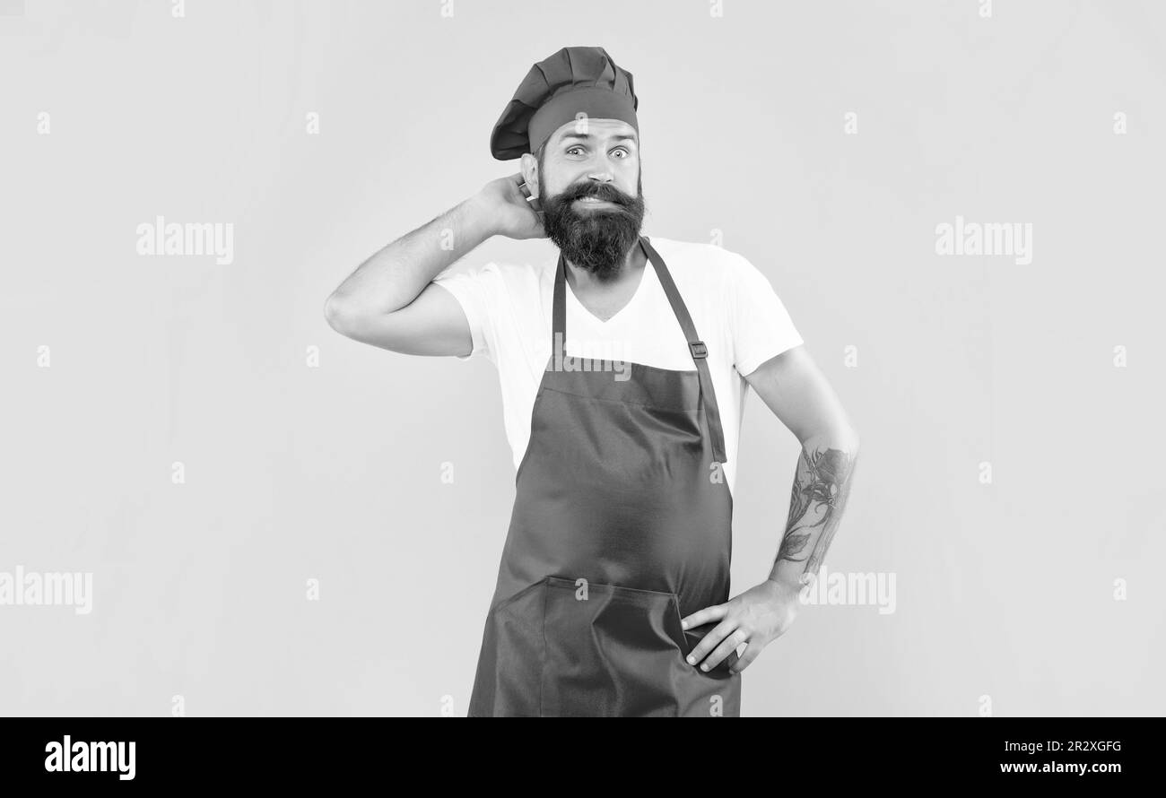 Hesitant man in red toque and apron scratching head yellow background ...
