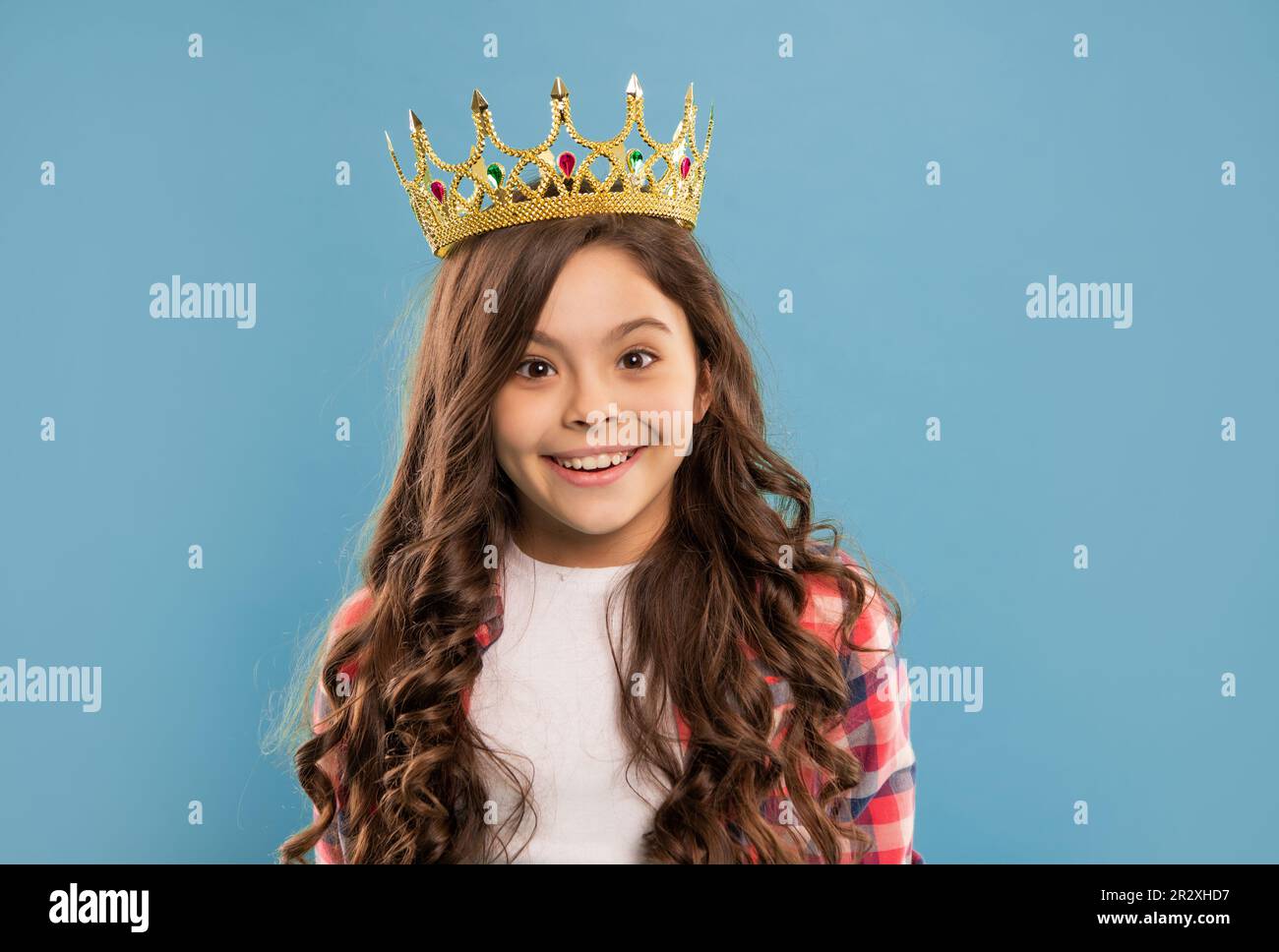 smiling child with curly hair in queen crown on blue background, smug ...