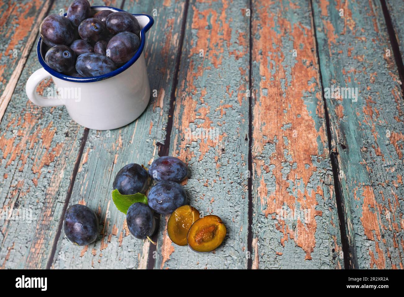 An enamel jug full of freshly harvested plums on old rustic wooden ...