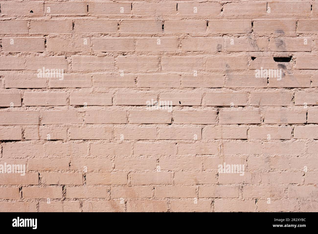 An old wall of different bricks painted in light red with some holes ...
