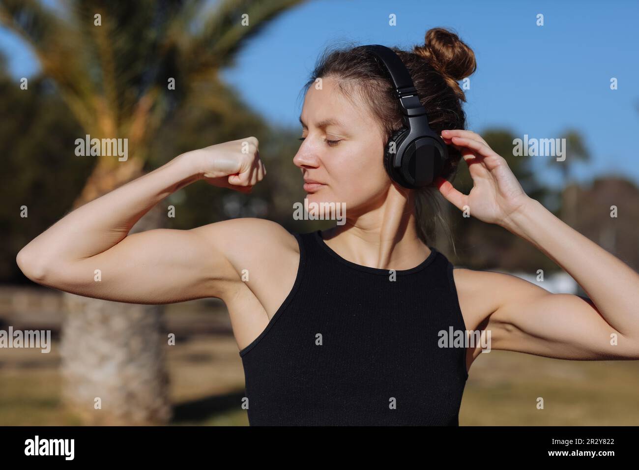 Young beautiful woman in sportswear raises arms to show muscles, biceps ...
