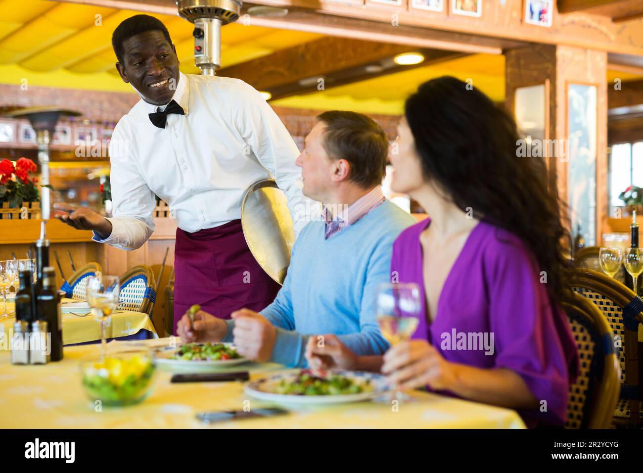 Positive biracial couple talking to friendly African American waiter in ...