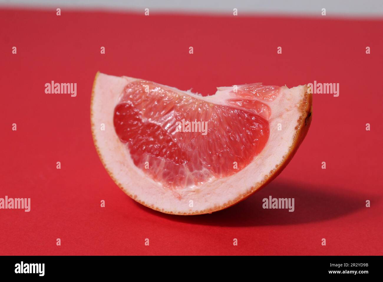 a piece of a slice of red grapefruit on a red background with a hard ...