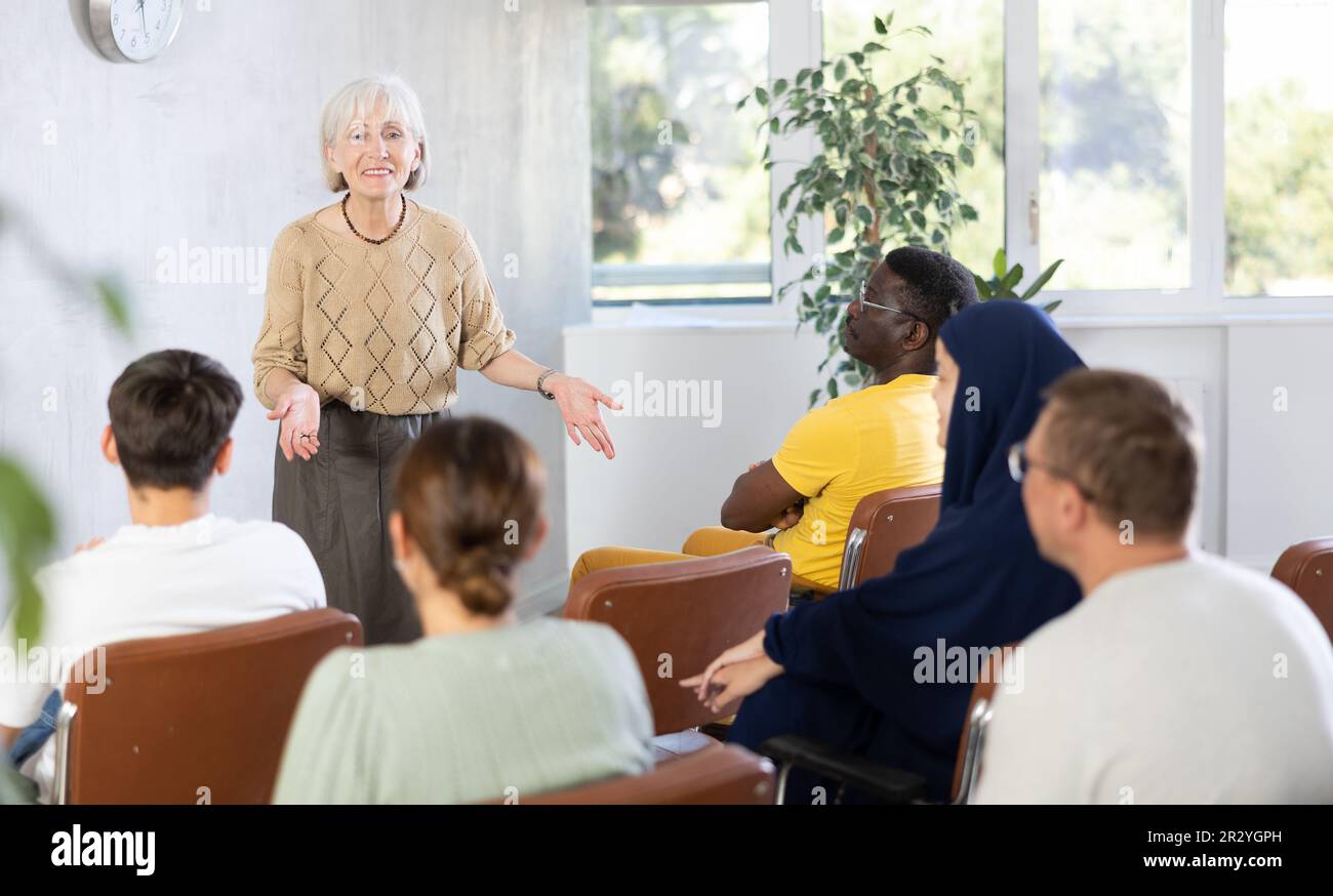 Mature female teacher giving lecture to group of multinational students ...