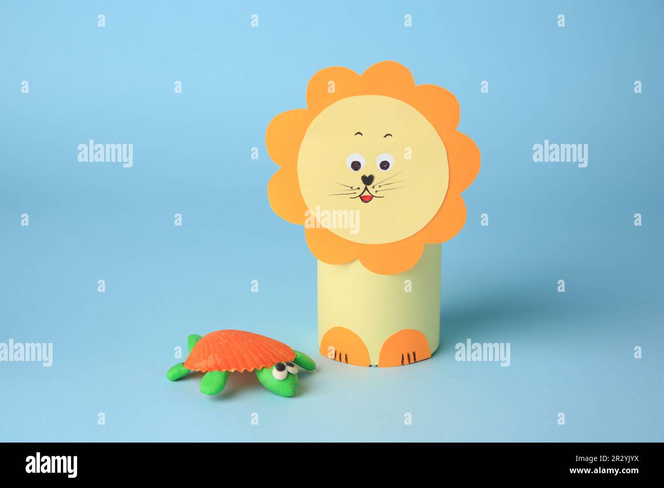 Toy lion made from toilet paper hub and plasticine turtle on light blue ...