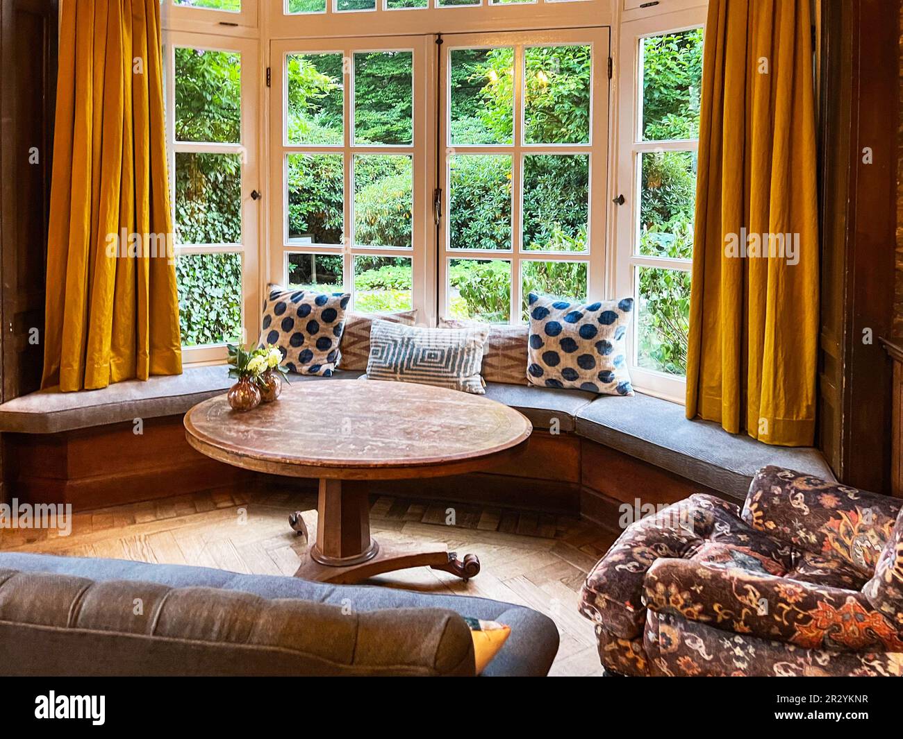 Wooden table near bay window seat with cushions in cozy room. Interior ...