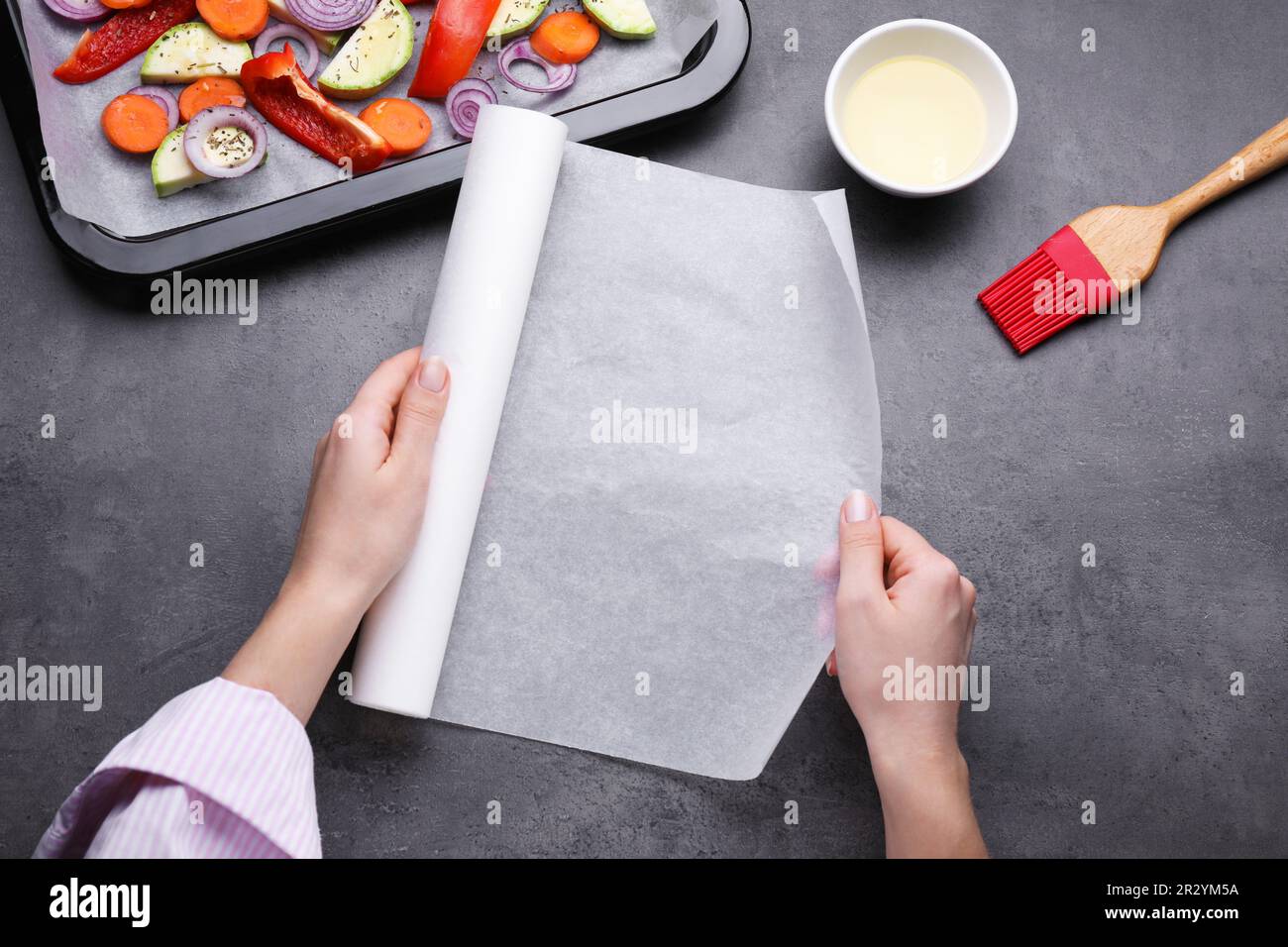 Woman holding parchment paper over dark grey table, top view. Baking ...