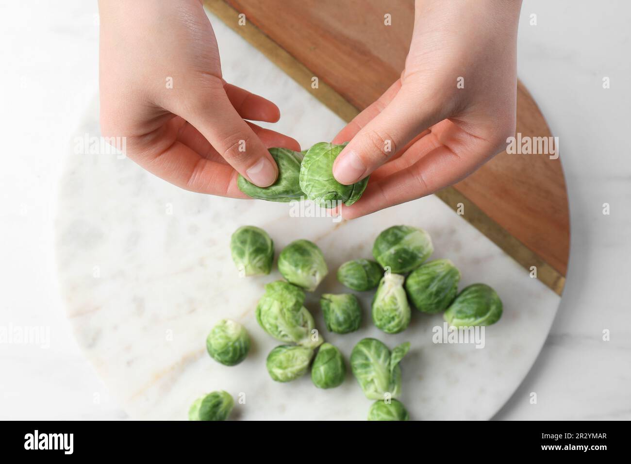Woman separating leaf from fresh brussel sprouts at white table, top ...