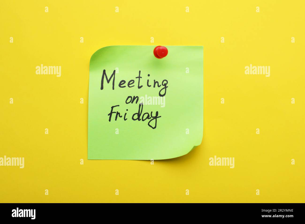 Paper note with words Meeting on Friday pinned to yellow background ...