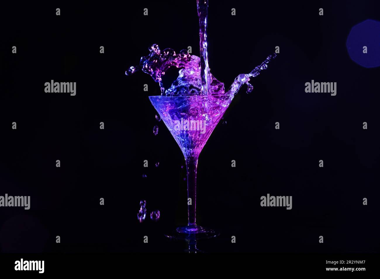 Pouring martini. Glass and splashes in neon lights on dark background ...