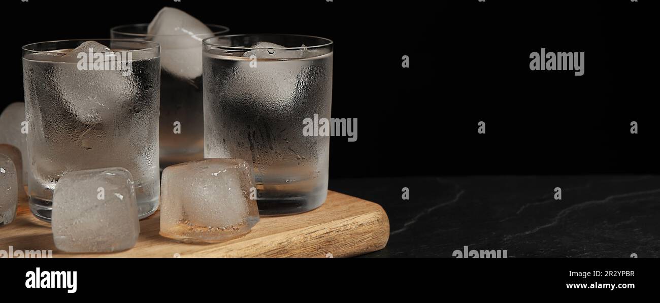 Shot glasses of vodka with ice cubes on black textured table, space for ...