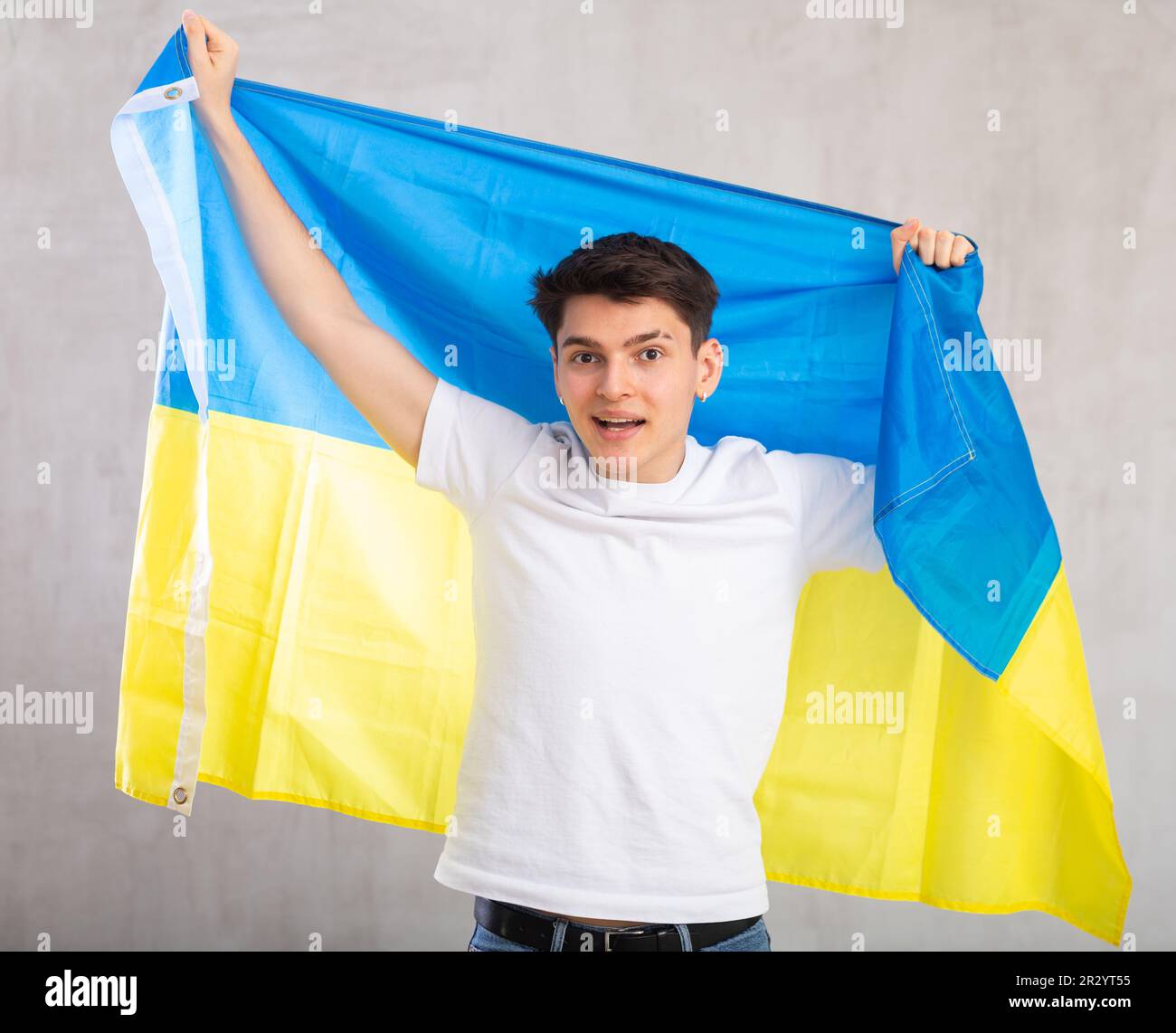 Confident positive young man holding a large national flag of Ukraine ...