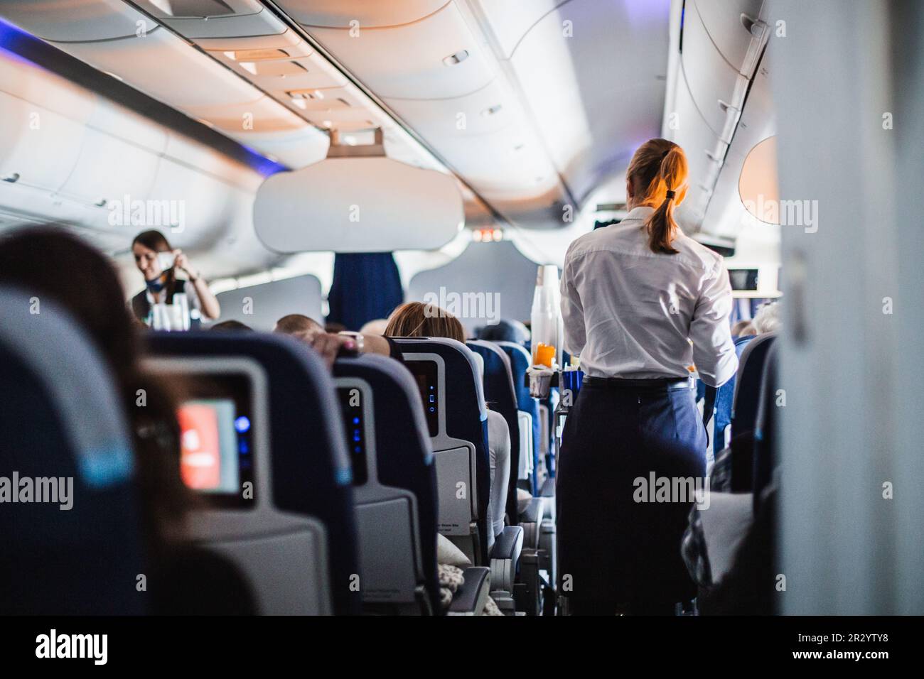 Interior of airplane with passengers on seats and stewardess in uniform ...